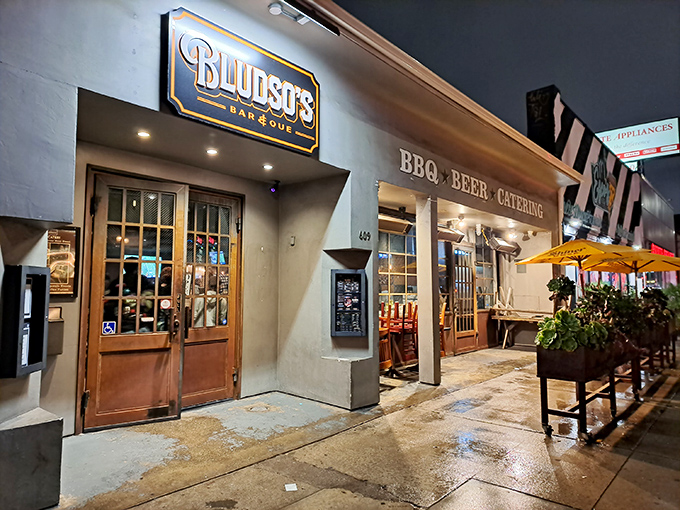 The iconic red storefront of Bludso's BBQ stands proudly on La Brea Avenue, a beacon for smoke-seekers with its no-nonsense signage and bright yellow umbrellas.