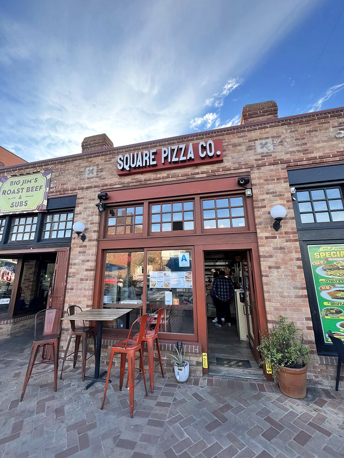 The brick facade of Square Pizza Co. stands like a temple to geometric perfection. Those orange chairs outside? Your invitation to pizza paradise.