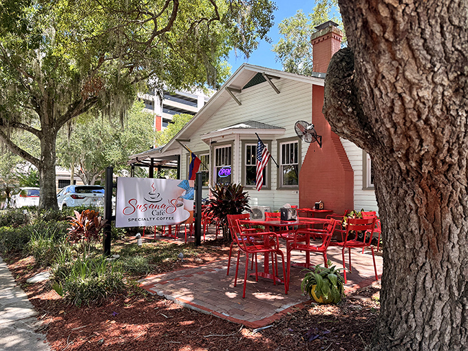 The charming cottage exterior of Susana's Cafe beckons with its vibrant red tables and lush surroundings, like a storybook setting for your next breakfast adventure.