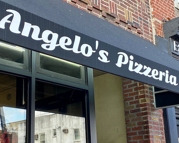 The unassuming storefront of Angelo's Pizzeria in South Philly, where culinary dreams come true behind that modest black awning.
