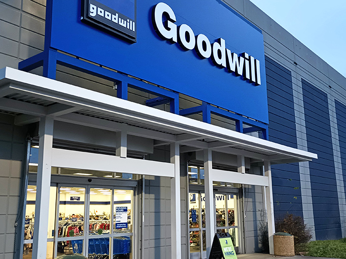 The iconic blue Goodwill sign beckons like a lighthouse for treasure hunters. Behind these doors, adventures await that can't be scheduled in a quick lunch hour.