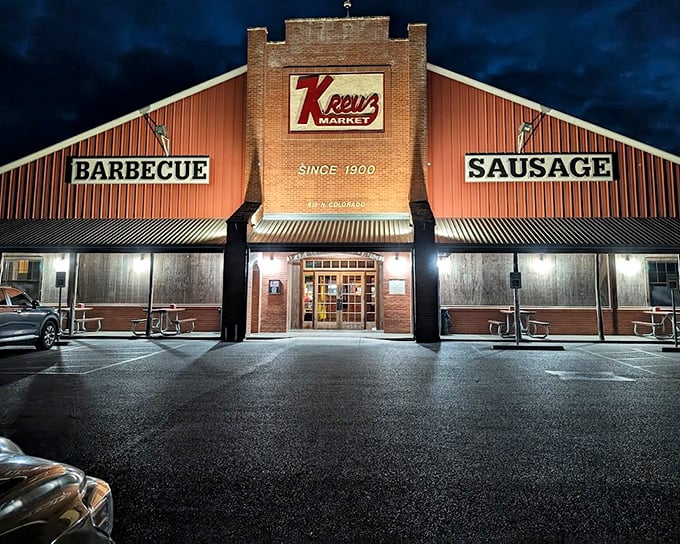The barbecue beacon of Lockhart stands tall against the night sky, its neon promise of "BARBECUE" and "SAUSAGE" calling to meat lovers like a smoky siren song.