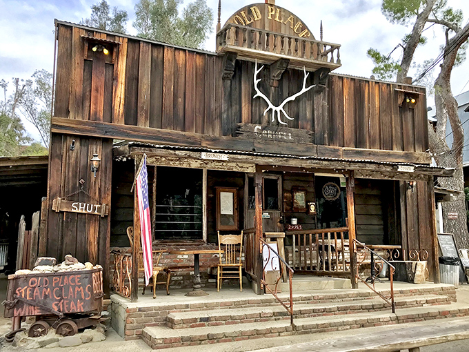 Like a movie set from a forgotten Western, The Old Place stands defiantly against time, its weathered wooden facade and American flag promising authentic frontier hospitality.