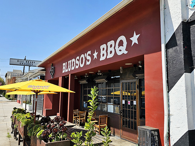 The iconic red storefront of Bludso's BBQ stands proudly on La Brea Avenue, a beacon for smoke-seekers with its no-nonsense signage and bright yellow umbrellas.