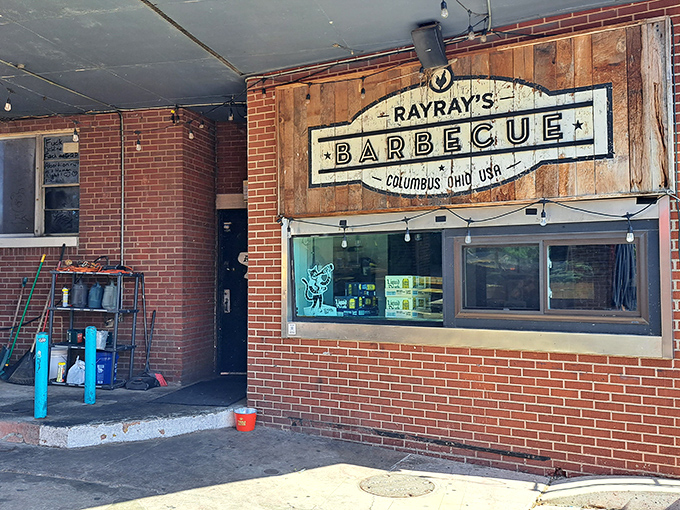 The rustic wooden sign against brick walls tells you everything you need to know: serious barbecue happens here, no frills required. 
