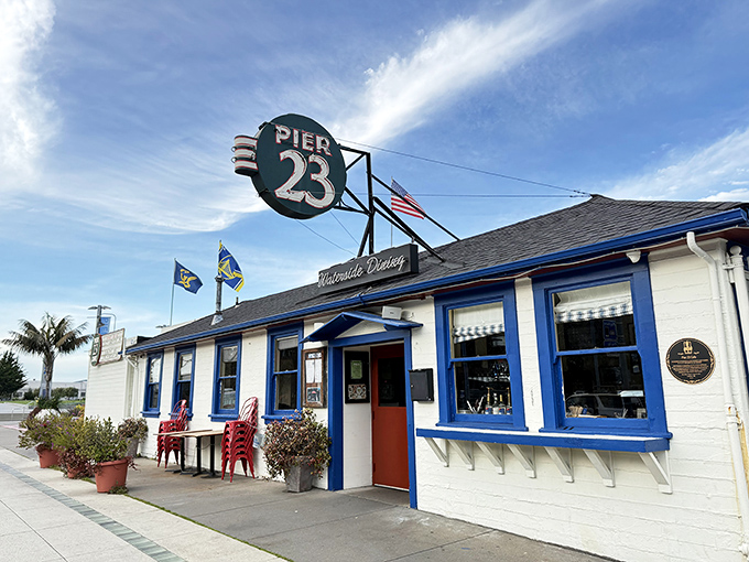The classic white-and-blue exterior of Pier 23 stands like a maritime postcard come to life, complete with those inviting red chairs that practically whisper, "Stay awhile."
