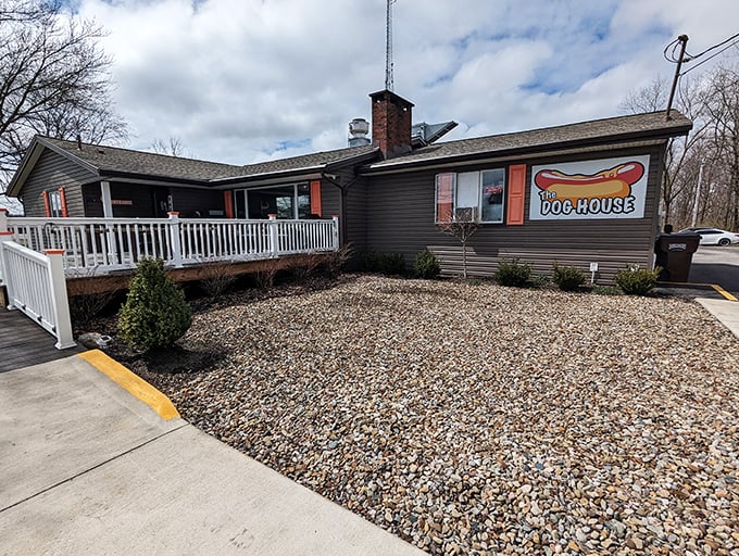 A ranch-style building with a white porch railing and colorful sign beckons like an old friend. This unassuming hot dog haven proves that culinary treasures often hide in plain sight.