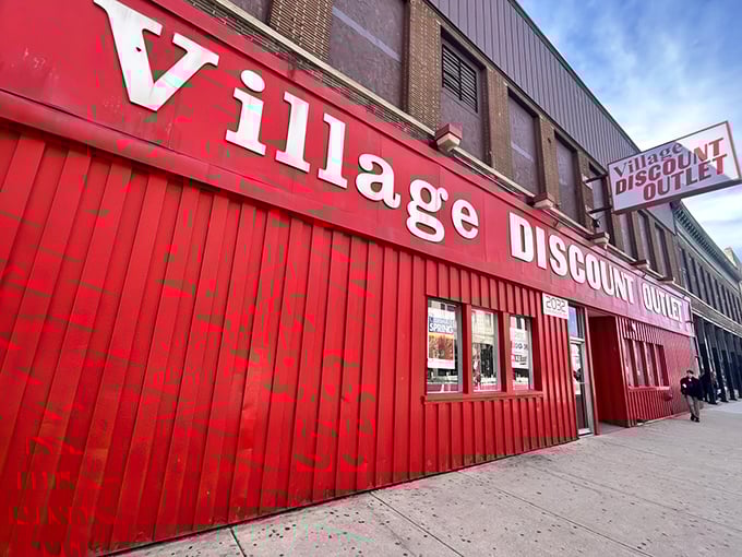 The crimson facade of Village Discount stands like a beacon for bargain hunters, its bold white lettering promising treasures within those no-frills walls.
