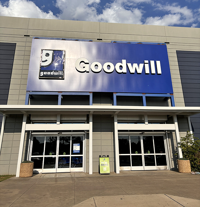 The iconic blue Goodwill sign beckons like a lighthouse for treasure hunters. Behind these doors, adventures await that can't be scheduled in a quick lunch hour.