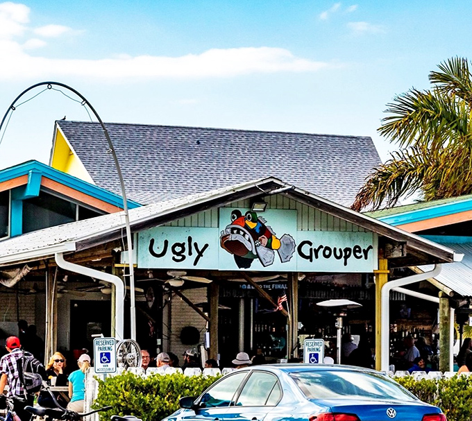 The colorful facade of The Ugly Grouper welcomes visitors with its whimsical cartoon mascot, promising a laid-back Florida dining experience unlike any other.