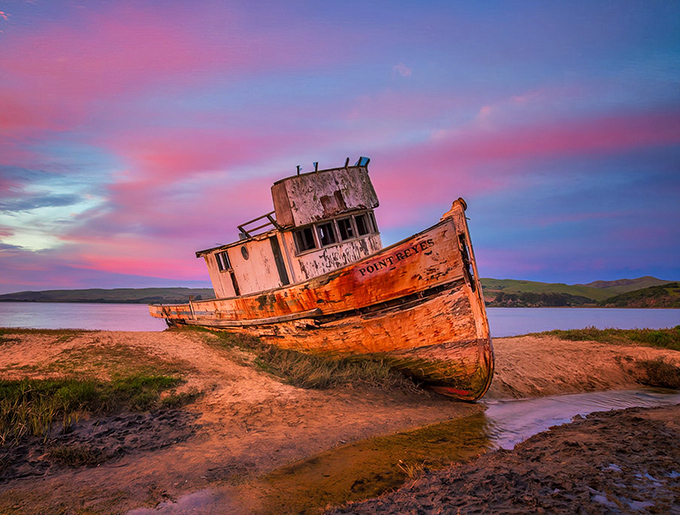 Nature's light show transforms the abandoned Point Reyes boat into a sunset masterpiece. The weathered hull glows like embers against the cotton candy sky.