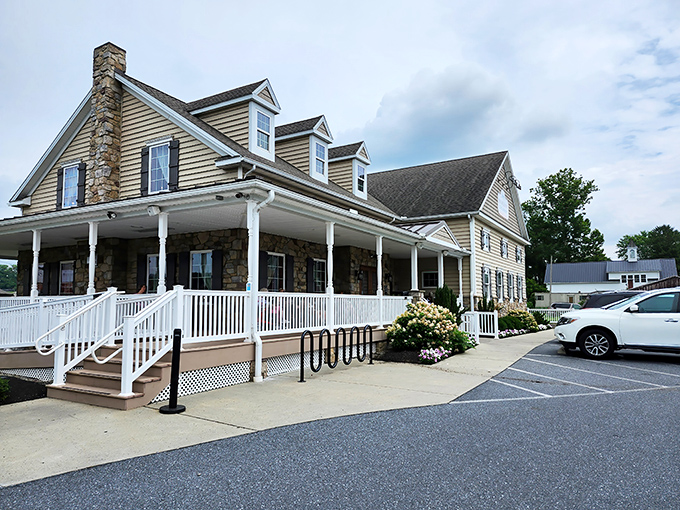 The farmhouse-style exterior of Fox Meadows Creamery welcomes visitors with its stone facade and inviting wraparound porch—architectural proof that calories consumed on rocking chairs don't count.
