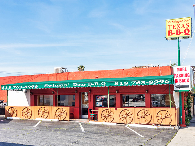 The bright red exterior of Swinging Door BBQ stands out like a beacon of hope for hungry travelers. Those wagon wheels aren't just for show—they're rolling you toward flavor town.