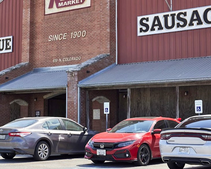 The barbecue beacon of Lockhart stands tall against the night sky, its neon promise of "BARBECUE" and "SAUSAGE" calling to meat lovers like a smoky siren song.