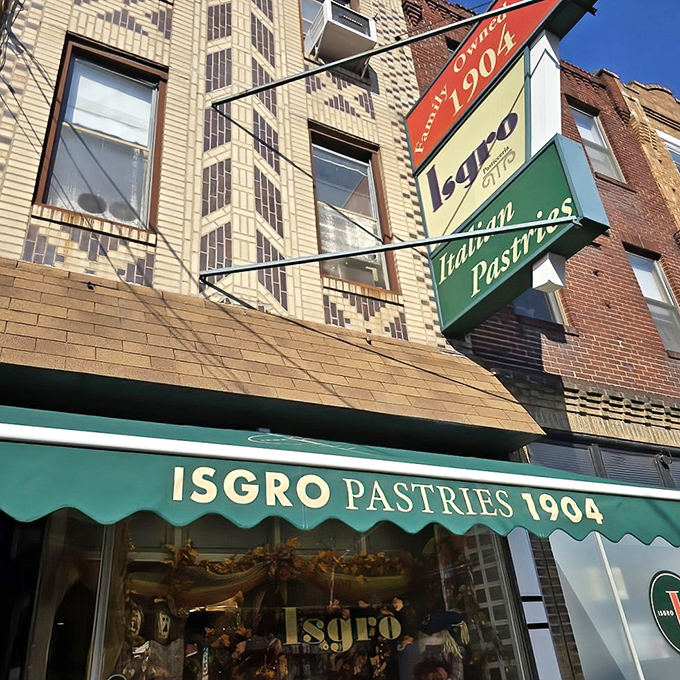The iconic red, cream, and green sign announcing Isgro's presence since 1904 - a beacon of sweetness on Christian Street's brick façade.