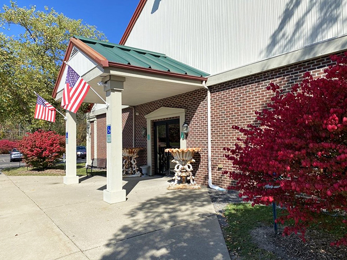 The welcoming entrance to I-76 Antique Mall, where American flags flutter in the breeze and vibrant red maples frame the doorway to nostalgia.