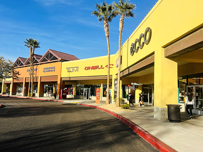 The outlet stores in Barstow, set against a clear blue sky, feature vibrant facades and bustling walkways where shoppers browse top-name brands in a lively, open-air atmosphere.