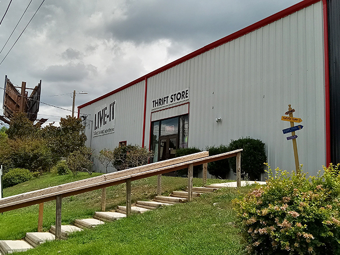 The unassuming exterior of LIVE-IT Thrift Store stands like a treasure chest waiting to be opened, complete with wooden ramp entrance and colorful directional sign.
