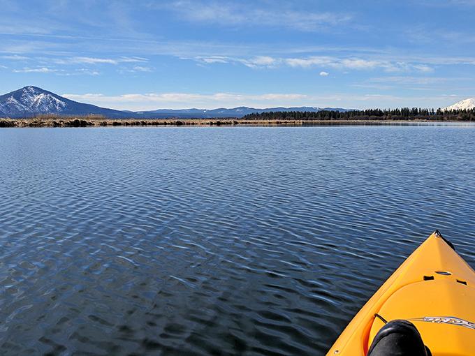Solitude perfected! A lone kayaker glides across mirror-like waters, with mountains creating nature's version of surround sound scenery.