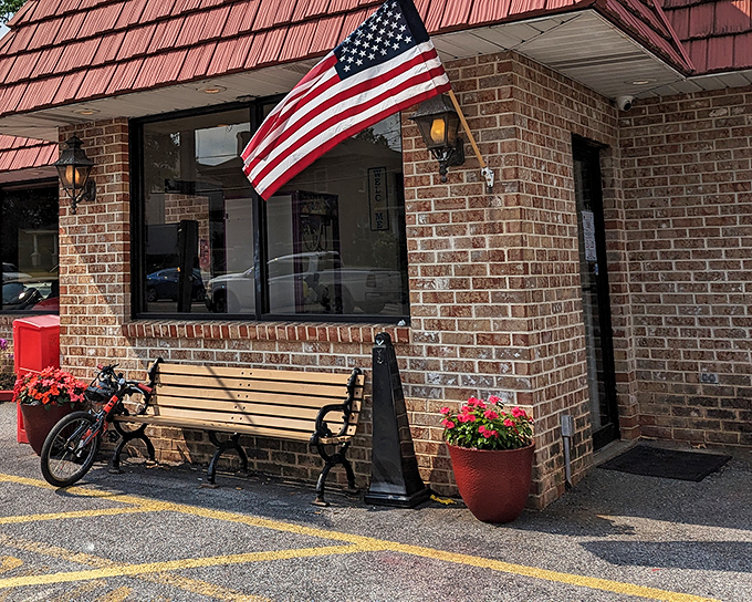 The American dream served daily: A charming brick exterior with patriotic flair, welcoming bench, and colorful flower pots that say "come on in, we've got something good cooking."