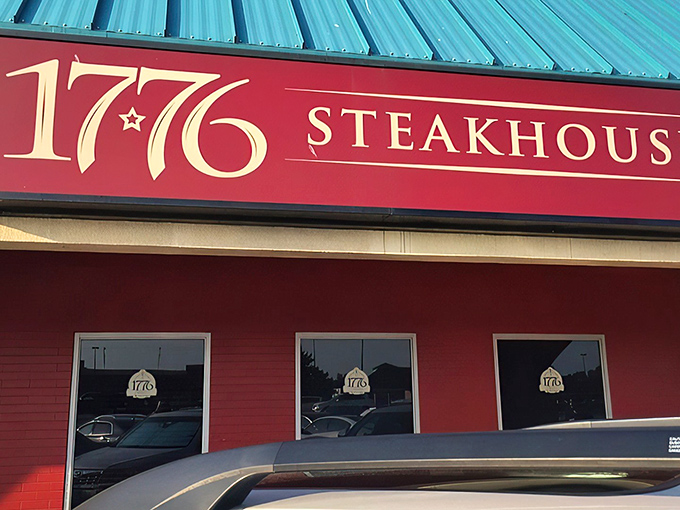 The glowing red sign of 1776 Steakhouse stands out like a beacon for hungry travelers, promising revolutionary flavors in an unassuming shopping center setting. 