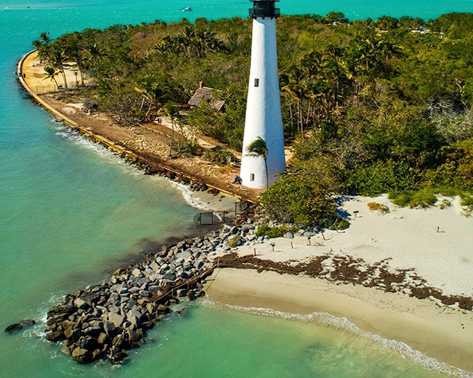 The Cape Florida Lighthouse stands like a sentinel from another era, its white tower gleaming against the turquoise waters that seem almost too perfect to be real.