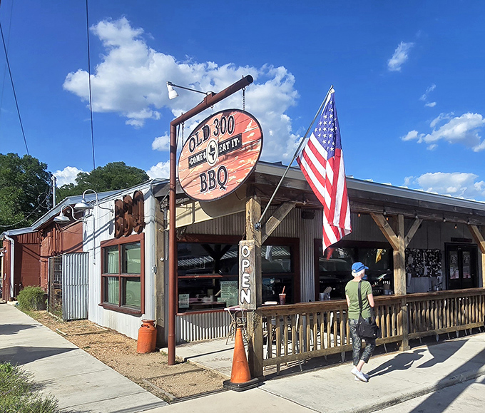 The Texas flag waves a hearty welcome outside Old 300 BBQ, where rustic wooden beams and corrugated metal promise authentic Hill Country hospitality.