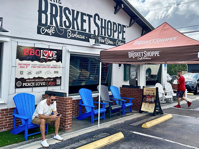 The white facade of The Brisket Shoppe beckons like a BBQ lighthouse, with those blue Adirondack chairs practically begging you to sit and savor.