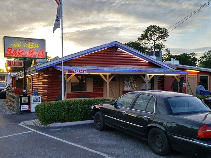 The rustic red exterior of Log Cabin BBQ stands as a beacon of comfort food in LaBelle, where Christmas lights twinkle year-round and promises of BBQ and seafood beckon hungry travelers.