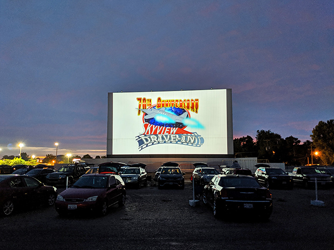 Twilight magic unfolds as the massive screen welcomes moviegoers. Nothing says summer nostalgia quite like cars gathered under a darkening sky.