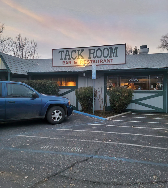 The unassuming exterior of Tack Room Bar & Restaurant, where vibrant foliage frames a sign that promises more than it shows—culinary magic awaits inside.