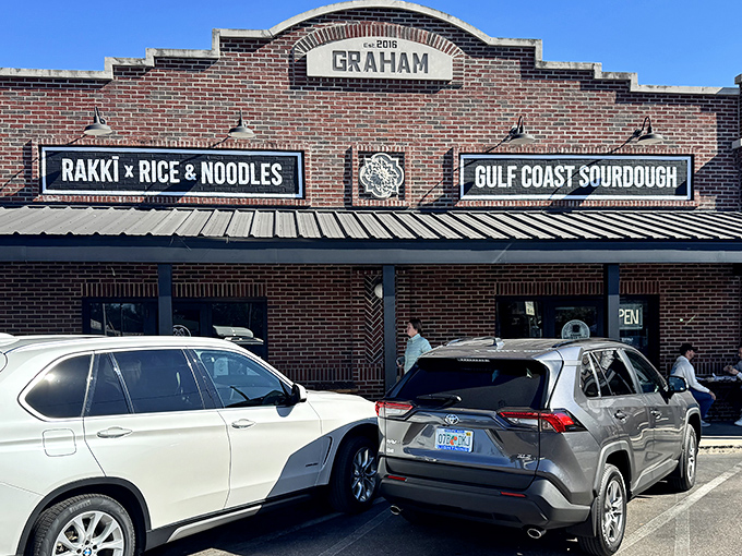 The Graham building stands like a brick-and-mortar food embassy, where Gulf Coast Sourdough's sign promises carb-laden diplomacy alongside its neighbor Rakki Rice & Noodles.
