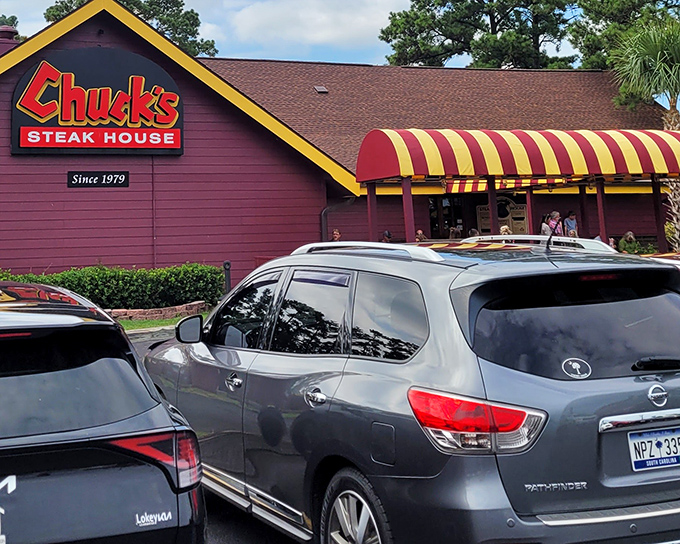 Chuck's exterior stands as a time capsule of steakhouse tradition, with its distinctive red-brown siding and cheerful yellow-striped awning beckoning hungry travelers.