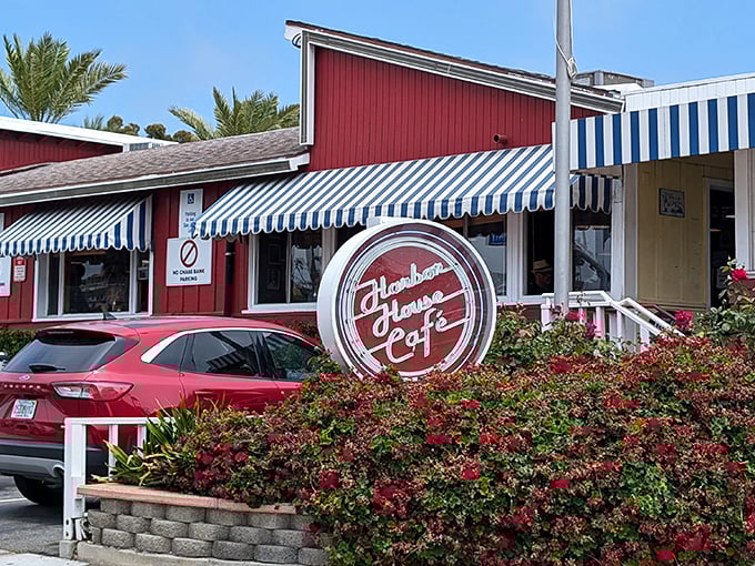 The iconic red exterior of Harbor House Cafe stands out like a beacon of comfort food hope along PCH, complete with those classic blue and white striped awnings.