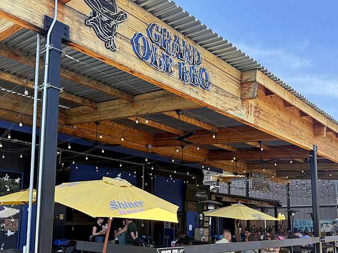 The rustic wooden facade of Grand Ole BBQ beckons like a smoke signal to barbecue pilgrims. Those yellow umbrellas aren't just for show&mdash;they're holding space for your BBQ dreams.