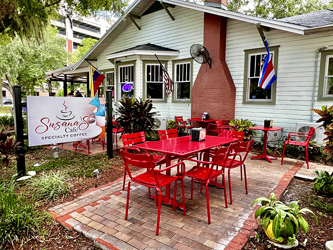 The charming cottage exterior of Susana's Cafe beckons with its vibrant red tables and lush surroundings, like a storybook setting for your next breakfast adventure.