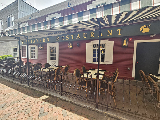 The iconic burgundy exterior of The Tavern stands as a beacon of culinary tradition in State College, complete with charming striped awnings and outdoor seating.
