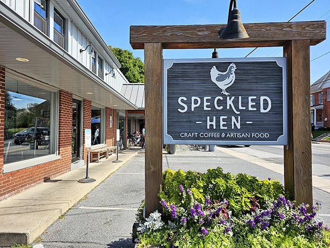 The welcoming wooden sign for Speckled Hen stands proudly amid vibrant flowers, promising craft coffee and artisan food in Strasburg's charming downtown setting.