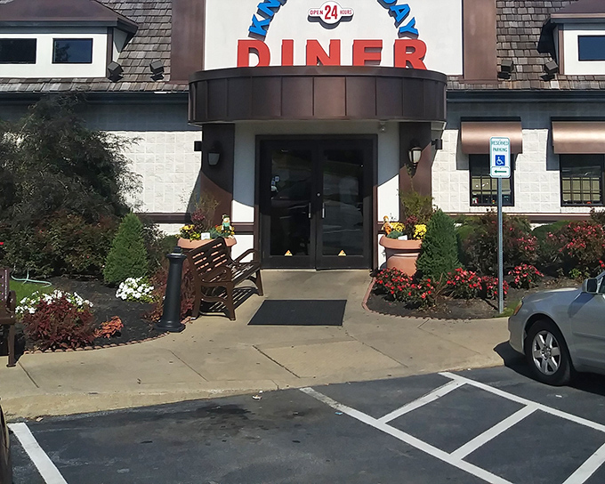 The classic diner entrance beckons with its no-nonsense charm. Colorful flower beds add a touch of warmth that says "come on in, we've been expecting you."