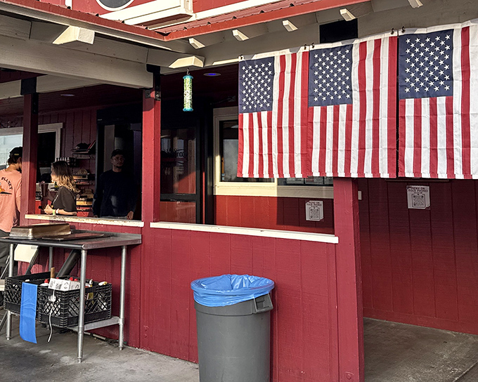 The patriotic red exterior of Copper Top BBQ stands as a beacon of hope for hungry travelers on Highway 395, American flags proudly announcing its barbecue allegiance.