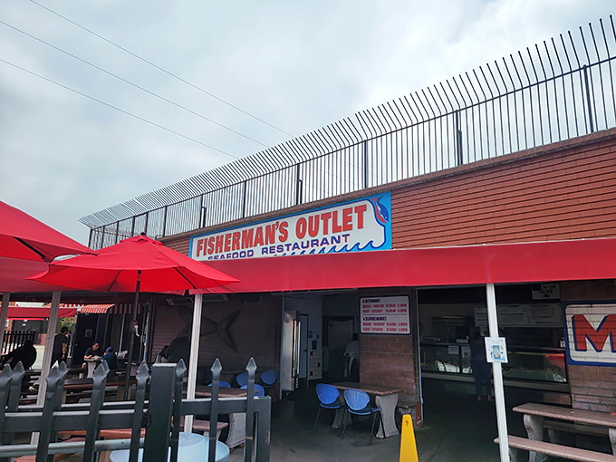 The unassuming exterior of Fisherman's Outlet, where those vibrant red umbrellas promise something special is happening beneath them. No fancy facade needed when the seafood speaks for itself.