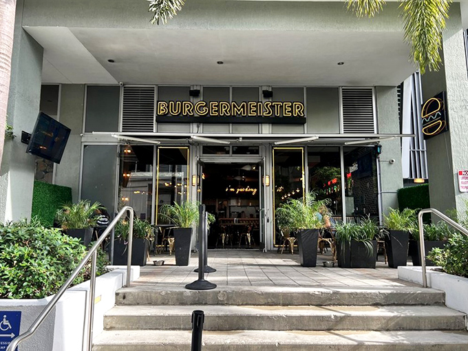 Burgermeister's glowing yellow sign beckons like a burger lighthouse amid the urban jungle of Brickell. Lush greenery frames the entrance, promising a tropical twist on comfort food.
