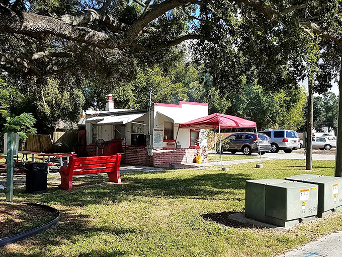 Simplicity at its finest: a modest white building with red trim, shaded by Florida oaks, promising smoky delights that need no fancy facade.