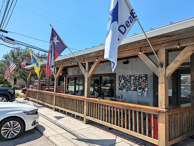 The Texas flag waves a hearty welcome outside Old 300 BBQ, where rustic wooden beams and corrugated metal promise authentic Hill Country hospitality.
