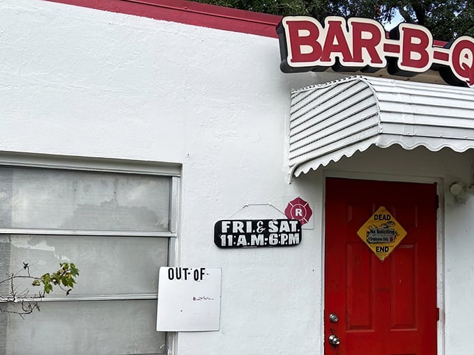 Simplicity at its finest: a modest white building with red trim, shaded by Florida oaks, promising smoky delights that need no fancy facade.