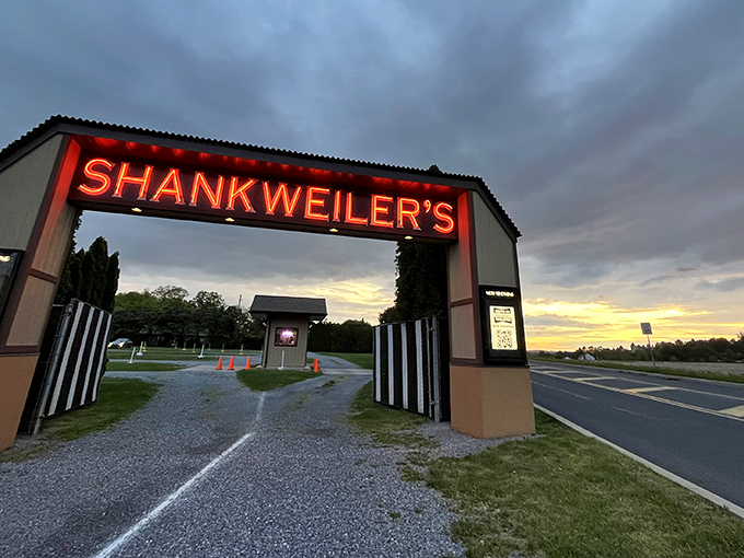 Modern cars line up facing the illuminated screen at dusk, where technology meets nostalgia under Pennsylvania's darkening sky.