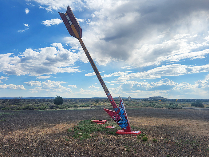 The iconic arrow pierces the Arizona sky like a relic from a forgotten road trip era, standing tall against the endless desert horizon.