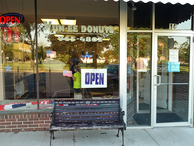 The unassuming storefront of Yum-Ee Donuts, complete with weathered bench, is like finding a treasure map where X marks the spot for deliciousness.