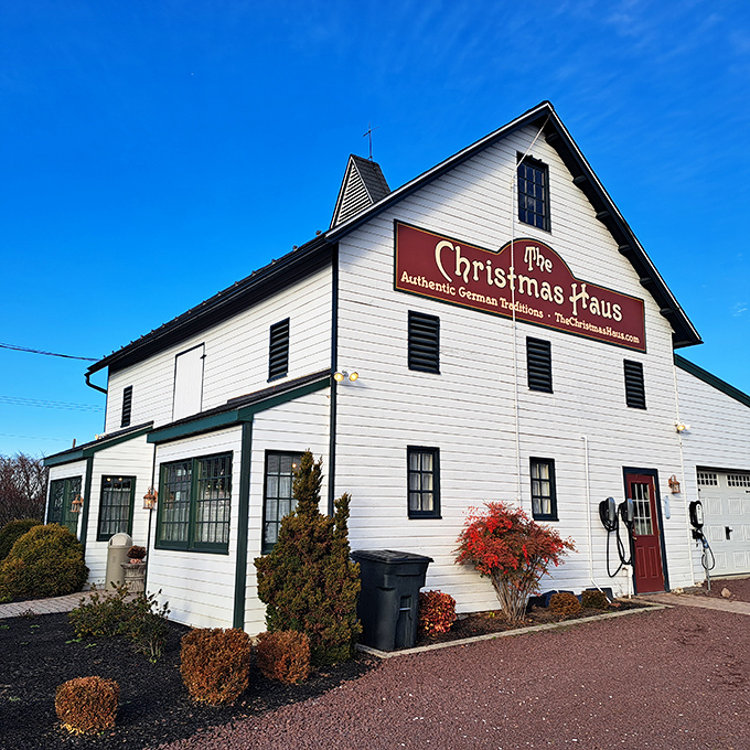 The white barn-like exterior of The Christmas Haus stands proudly against a blue Pennsylvania sky, its red sign promising year-round holiday magic.