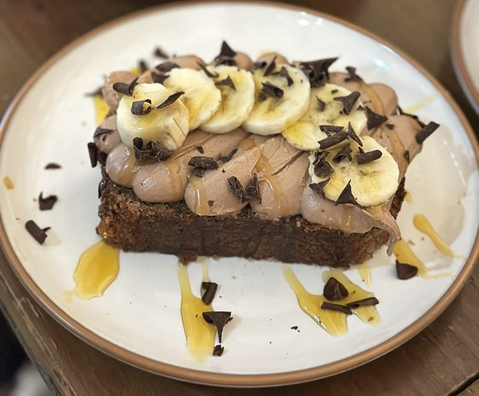 Banana bread elevated to art form: topped with chocolate shavings, fresh banana slices, and what appears to be a caramel drizzle that's making my screen look lickable.